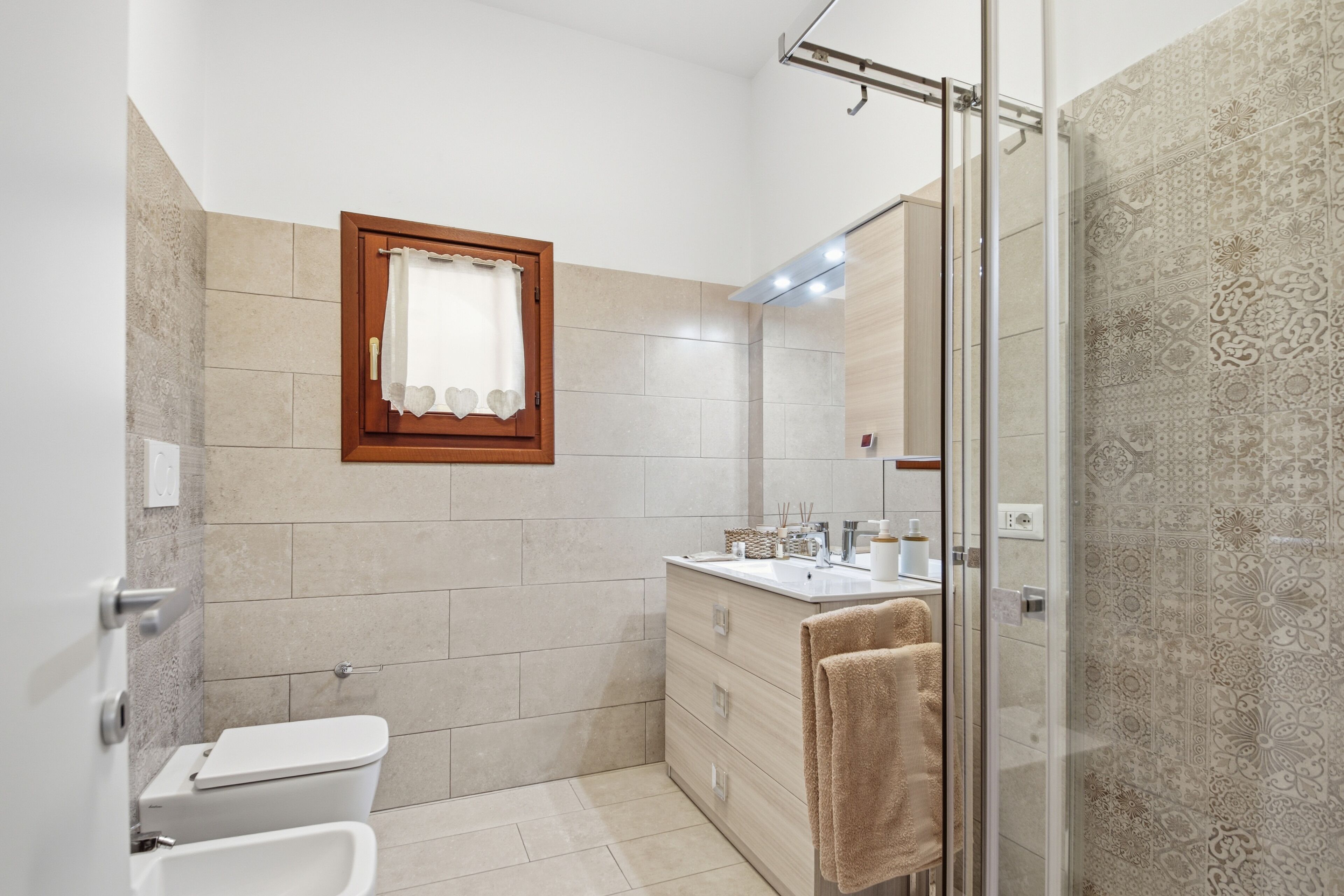 Uma casa de banho moderna com sanita, bidé, toucador com espelho e zona de duche.