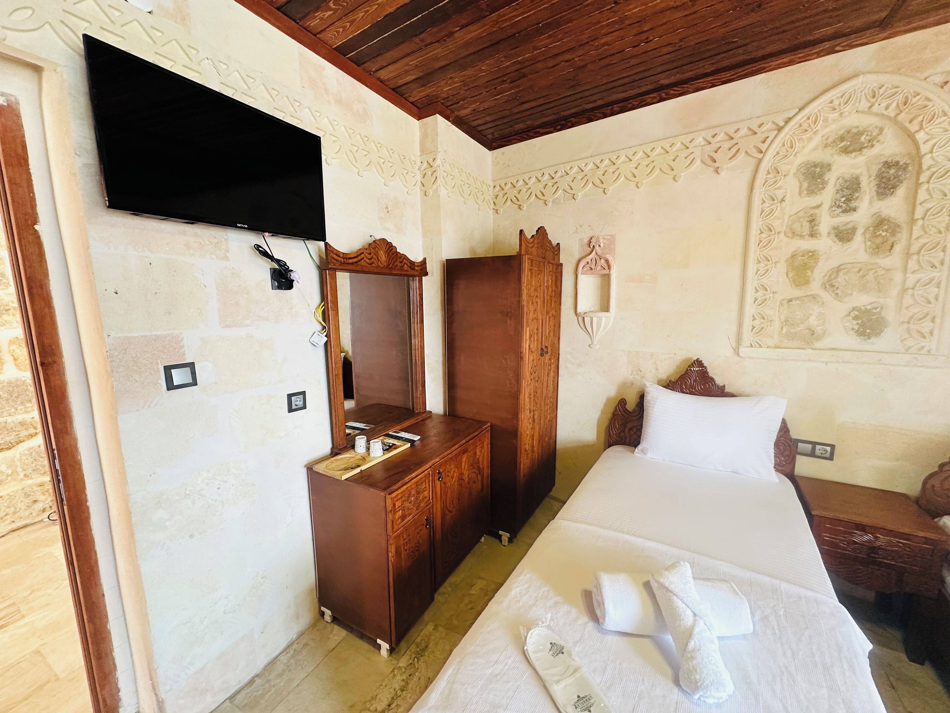 Quarto de hotel com uma cama, cómoda de madeira, toucador com espelho, televisão de ecrã plano na parede e painel decorativo.