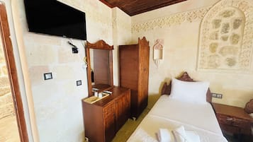 Quarto de hotel com uma cama, cómoda de madeira, toucador com espelho, televisão de ecrã plano na parede e painel decorativo.