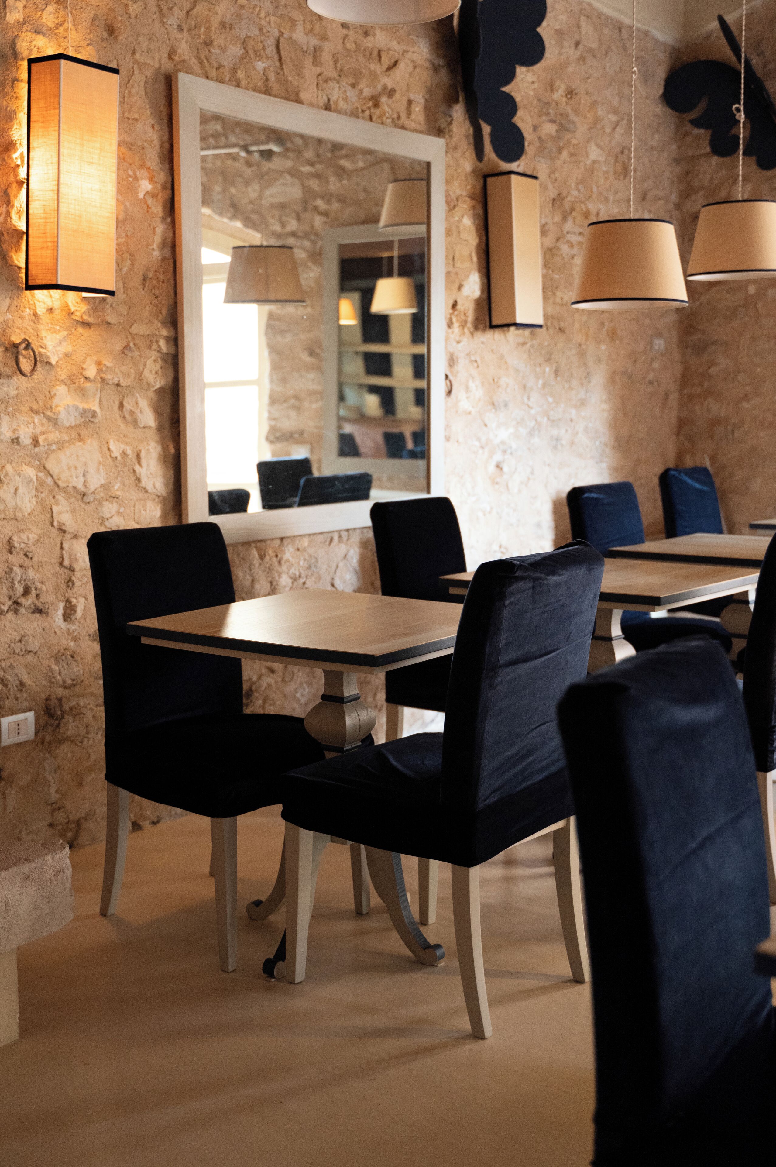 Uma sala de jantar com parede de pedra, um espelho grande e luminárias pendentes.