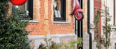 Um edifício com placa indicando um bar de comida e hotel. Há plantas em vasos e uma scooter vermelha estacionada na frente.