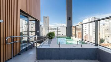 Piscina no terraço com barreira de vidro, guarda-corpos de metal e vista dos edifícios ao redor.