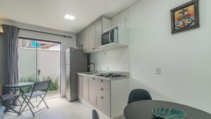 Cozinha compacta com geladeira, micro-ondas e fogão a gás. Há uma área de jantar com mesa e cadeiras.