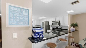 Uma cozinha moderna com armários brancos, bancada preta e um espaço bar com banquetas.