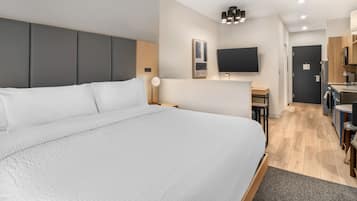 Quarto de hotel moderno com cama grande, escrivaninha, televisão de tela plana e cozinha compacta.