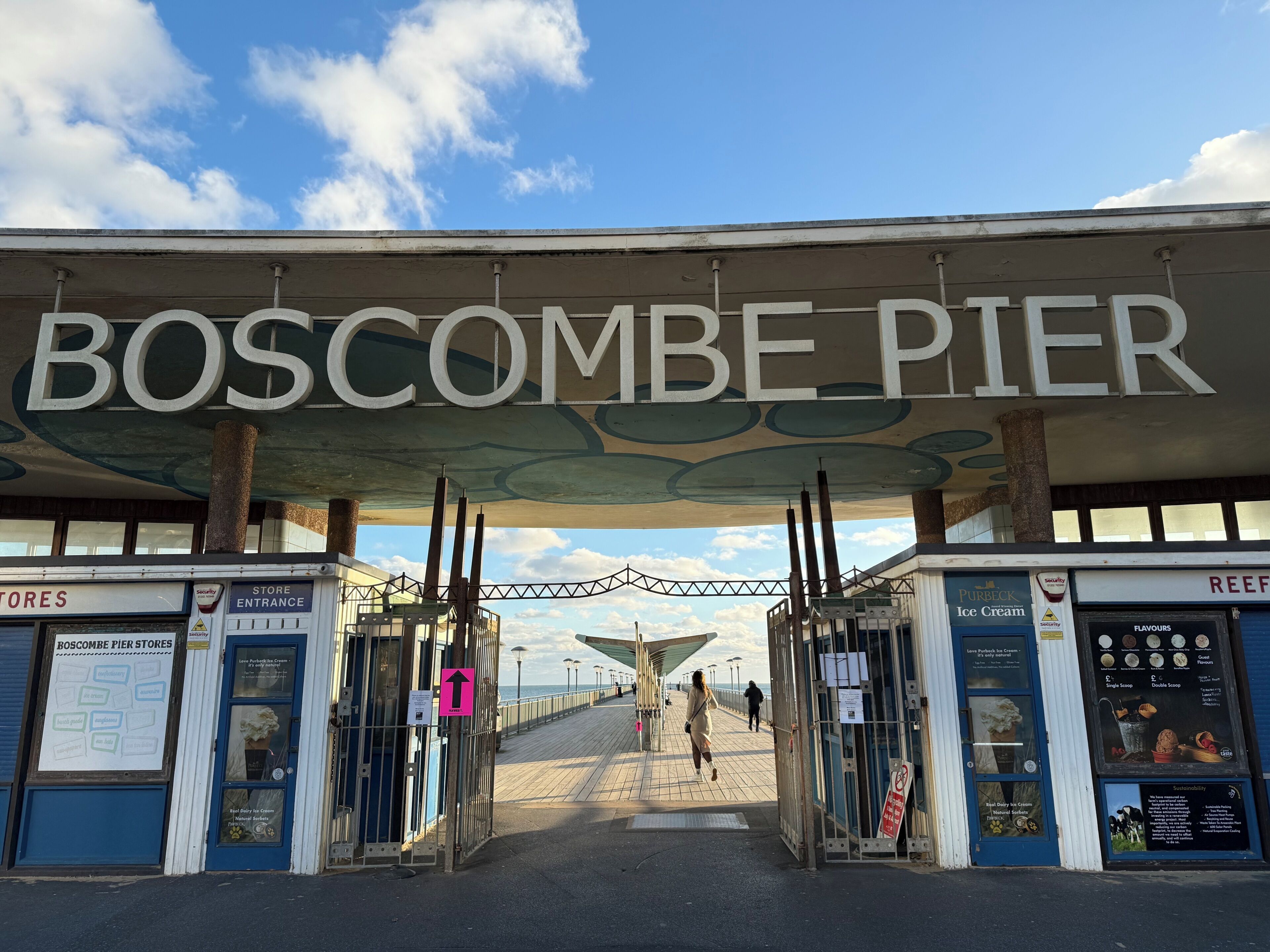 A entrada do Pier de Boscombe, com uma placa que diz 'BOSCOMBE PIER' e um portão de entrada azul.