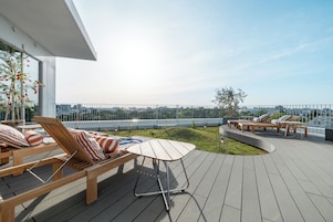 Terraço no telhado com espreguiçadeiras de madeira, uma pequena mesa e vista para a paisagem urbana.