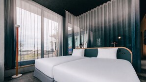Quarto de hotel com uma cama grande, um abajur e vista para o exterior.