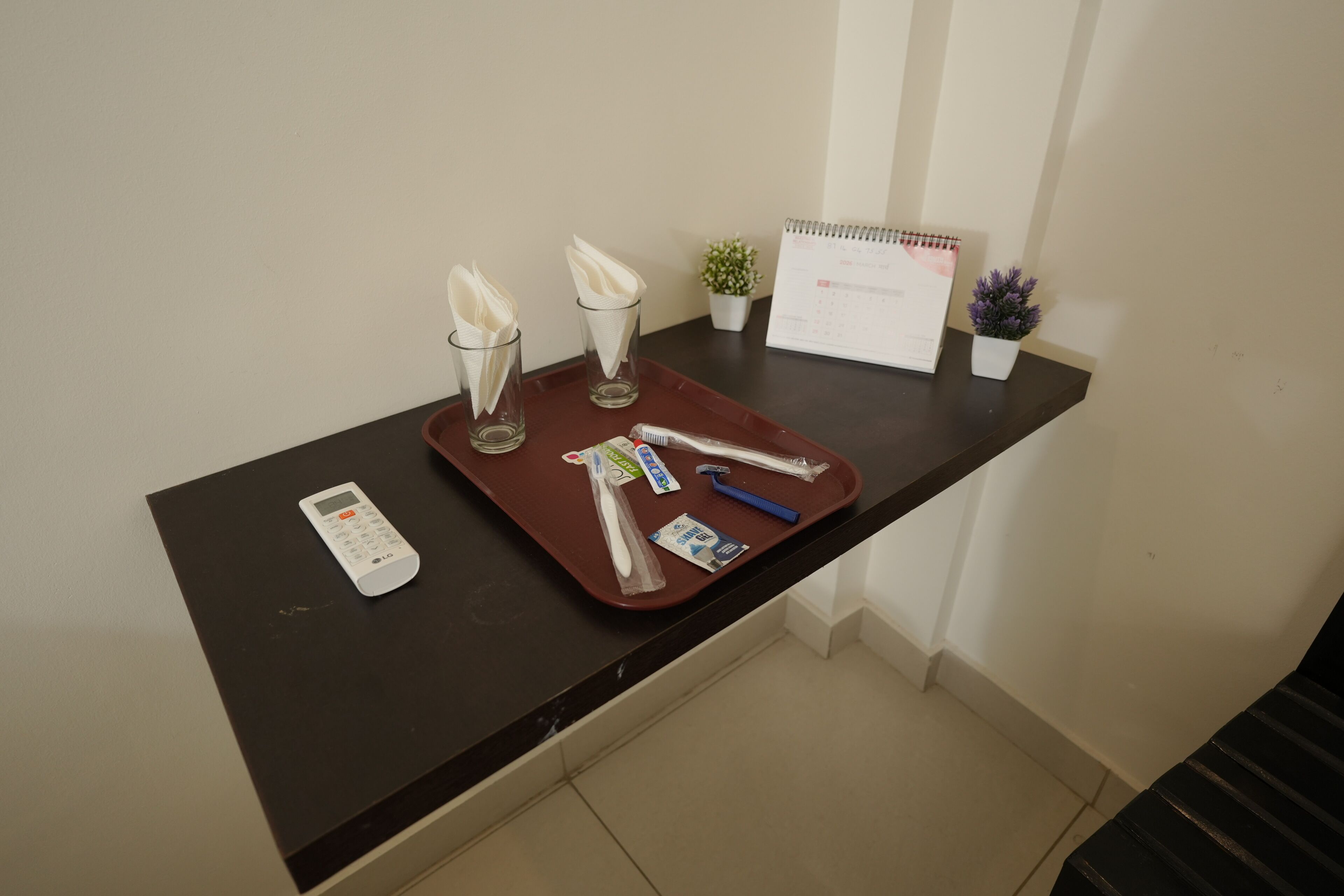 Mesa com controle remoto, bandeja com guardanapos, calendário e uma pequena planta em vaso.