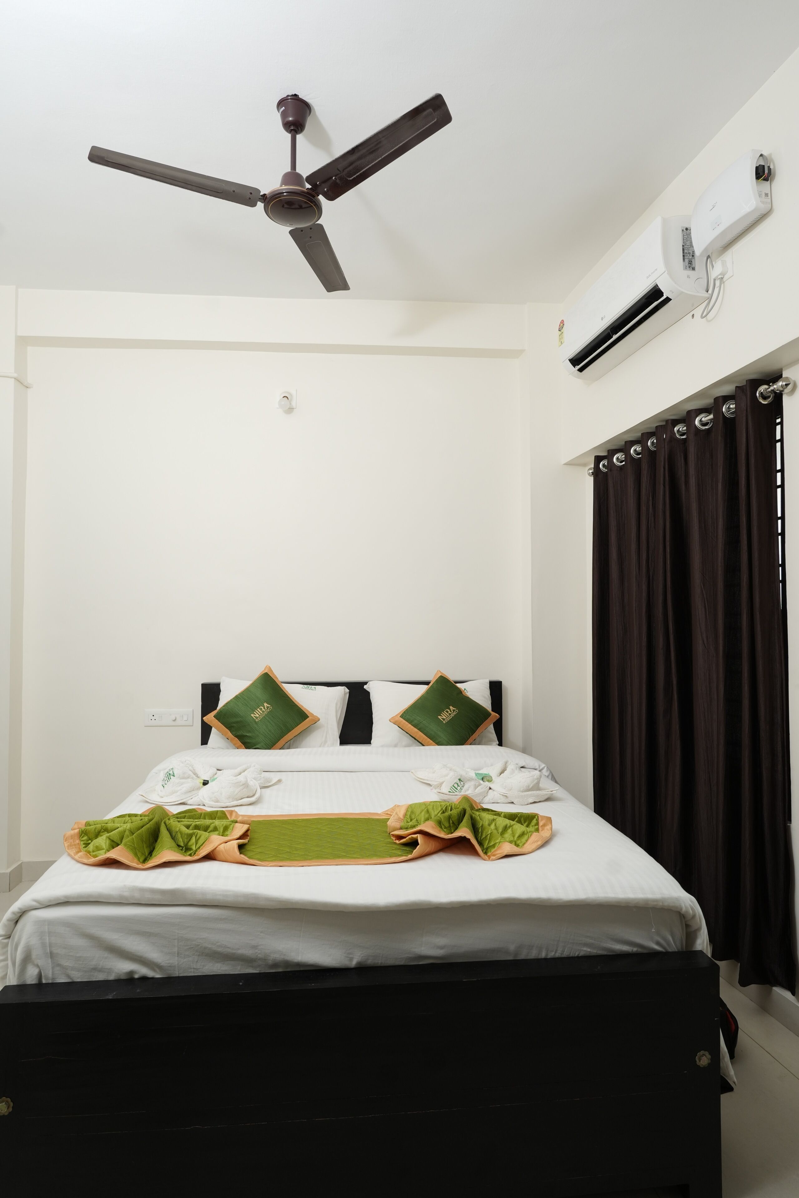 Quarto de hotel com cama, ventoinha no teto, aparelho de ar condicionado e janela com cortinas.