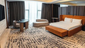 Quarto de hotel moderno com uma cama grande, uma mesa pequena, uma cadeira e um sofá.