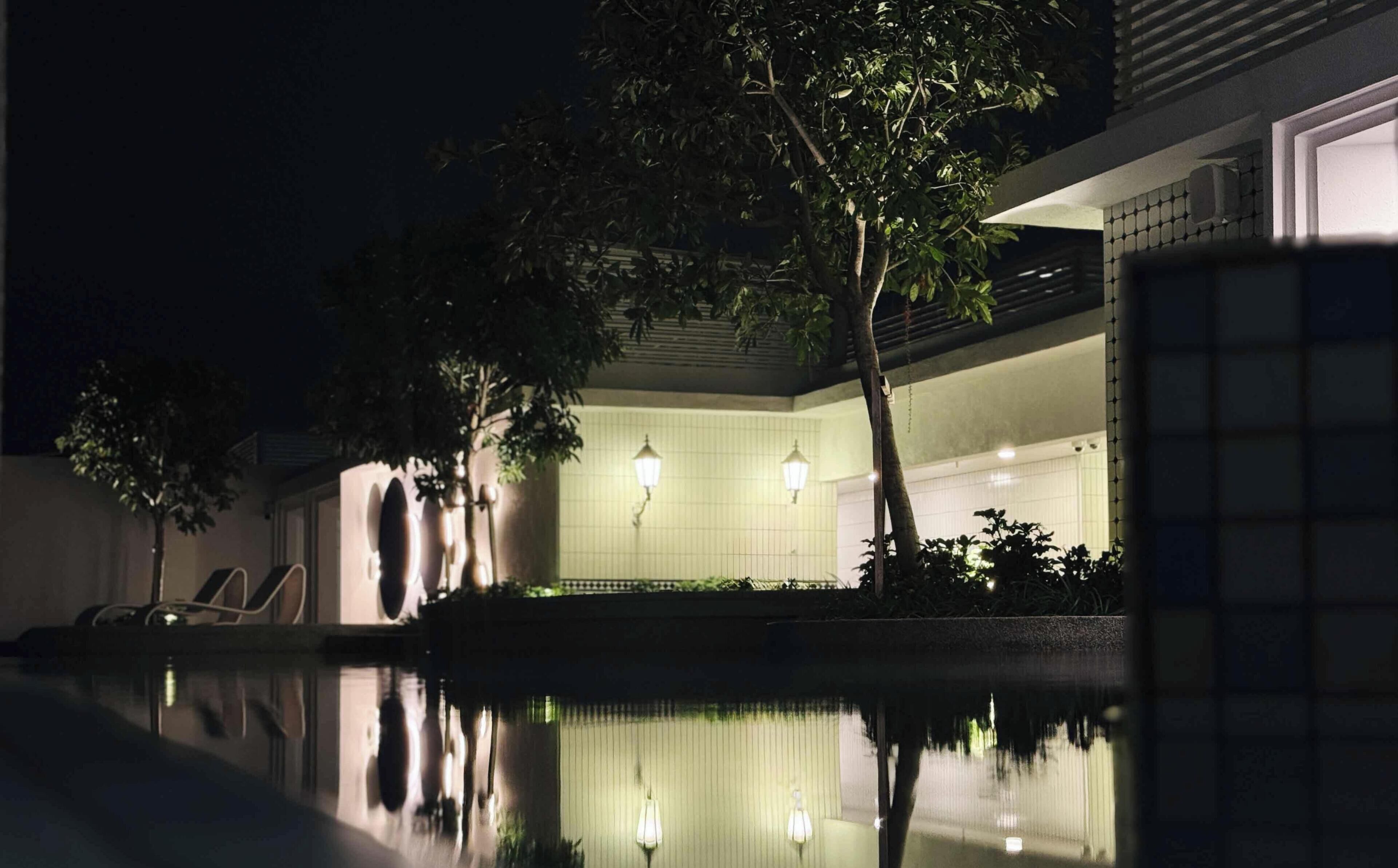 Um edifício moderno com piscina, árvores e duas luminárias de parede iluminadas.