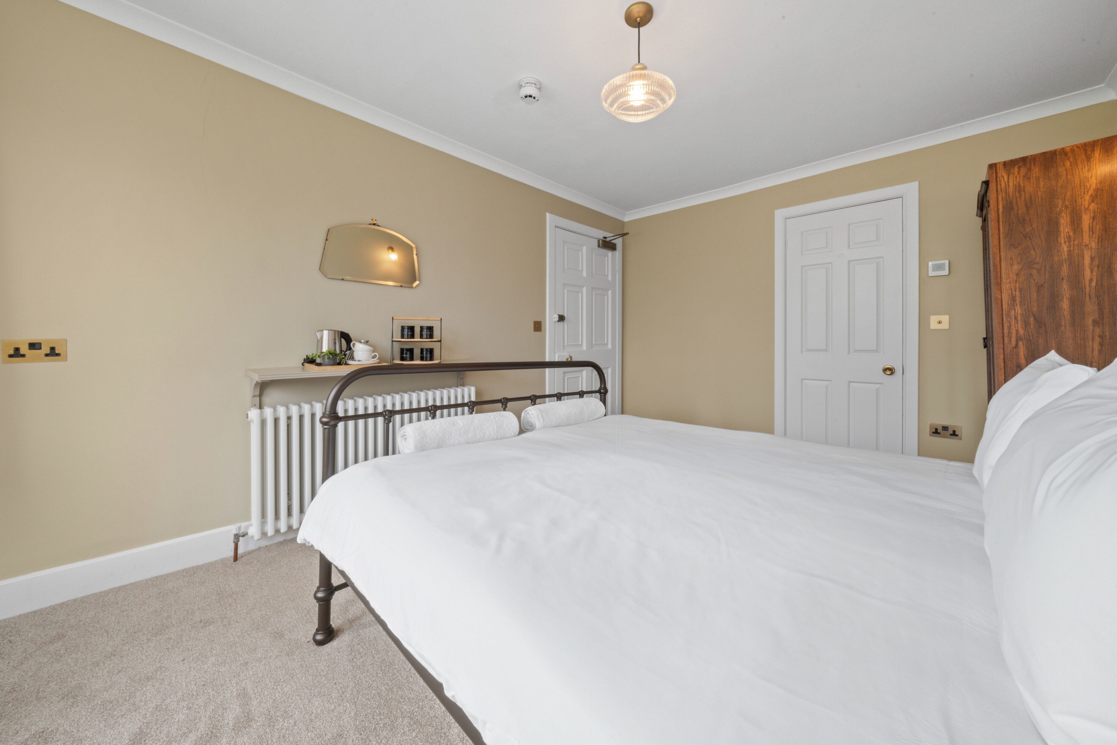 Quarto com uma cama grande, um radiador, uma porta branca e um guarda-roupa de madeira.