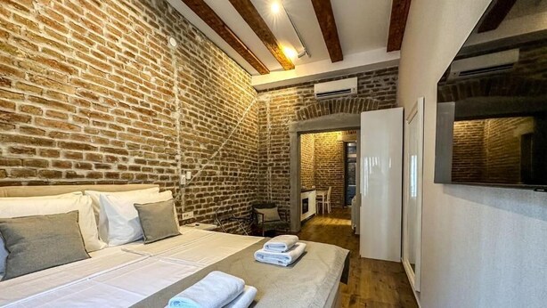 Um quarto com parede de tijolos, cama com roupa de cama branca e piso de madeira.