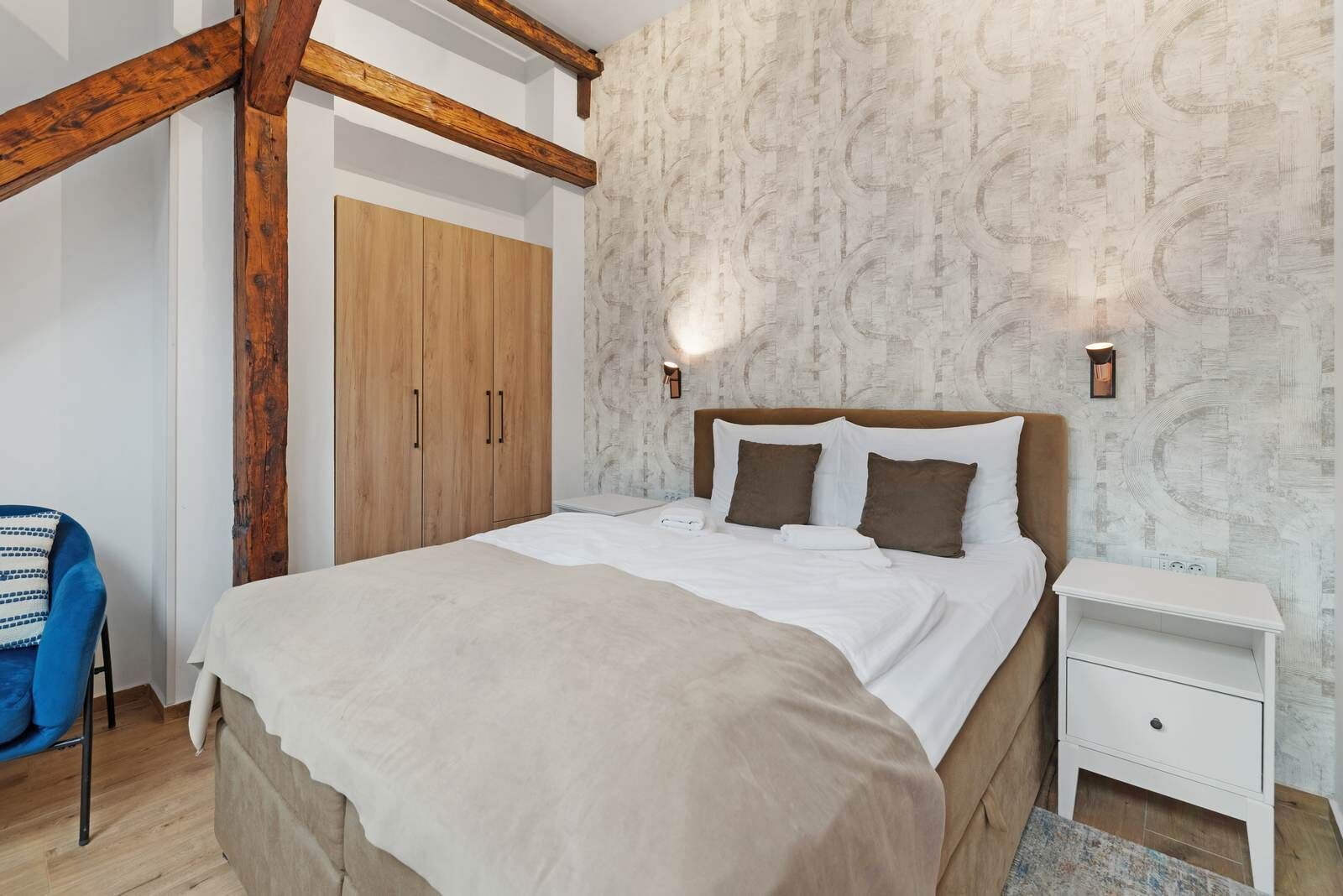 Quarto com teto de madeira, cama com roupa de cama branca, mesa de cabeceira e guarda-roupa.