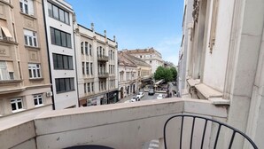 Uma varanda com vista para uma rua repleta de edifícios, uma cadeira e uma mesa.
