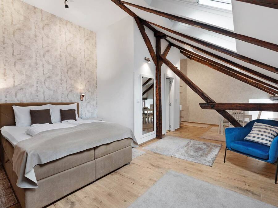 Quarto com cama, mesa de cabeceira, uma cadeira azul e escada que leva a um andar superior.