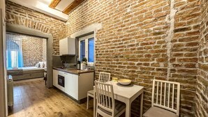 Uma cozinha compacta com parede de tijolos, piso de madeira e área de refeições com cadeiras brancas.
