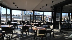 Um restaurante moderno com grandes janelas, mesas ao ar livre e vista para uma obra.