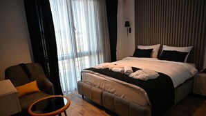 Quarto de hotel com uma cama grande, uma cadeira, uma mesinha e uma mesa de cabeceira.