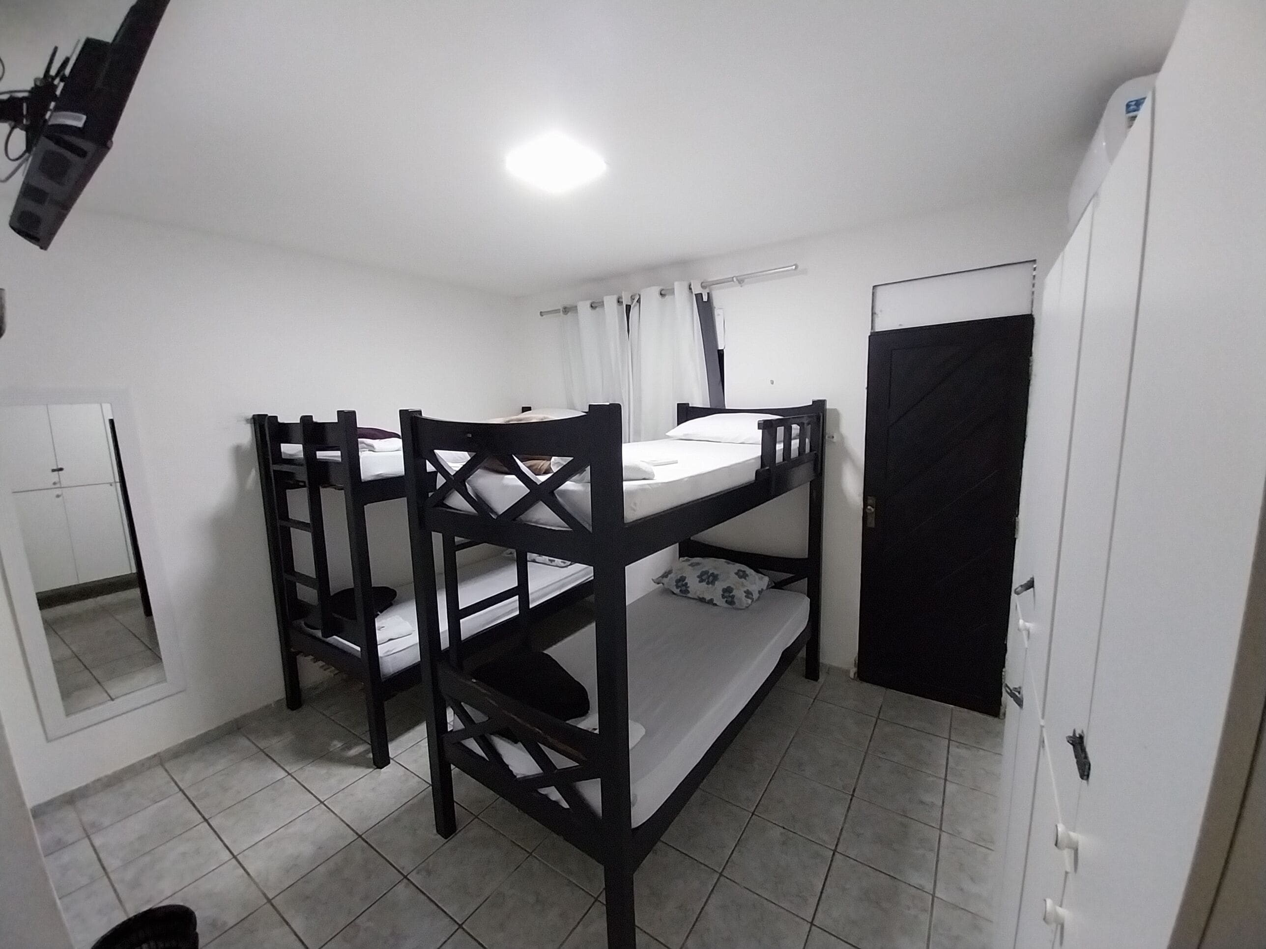 Quarto com beliche, espelho, guarda-roupa e porta.