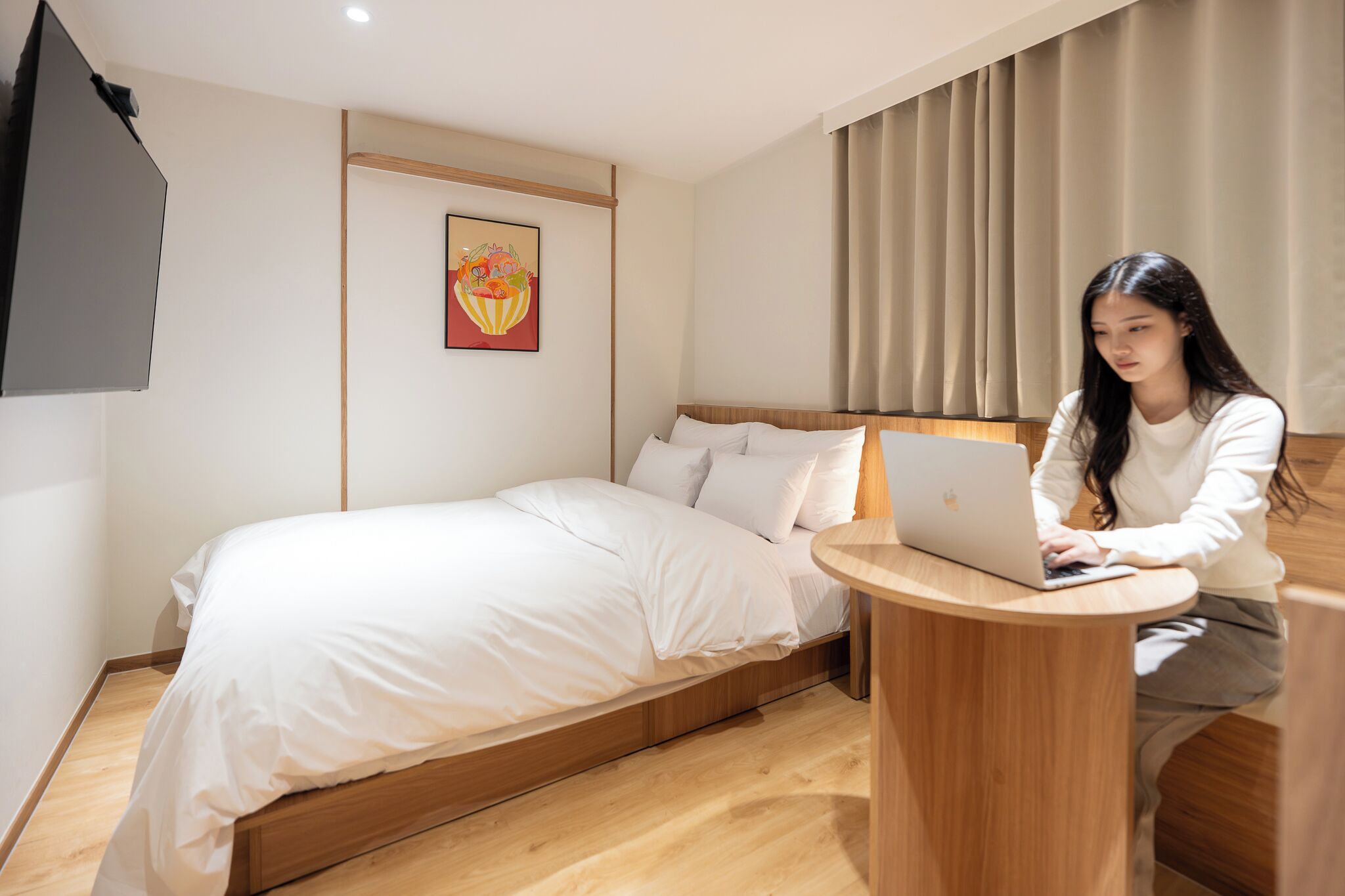Quarto de hotel com uma cama, uma mesa redonda de madeira e um computador portátil.