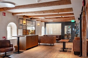 Interior moderno com vigas de madeira aparentes, área de bar, assentos e sinalização de saída visível.