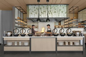 Uma cozinha moderna com dois chefs a cozinhar, prateleiras com utensílios de cozinha e uma parede com tema de bambu.