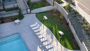 Uma área de piscina no terraço com espreguiçadeiras, um pequeno gramado e uma escadaria que dá acesso a um nível superior.