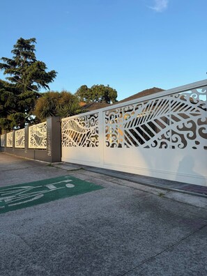 Uma cerca branca decorativa com desenhos recortados detalhados, uma faixa de bicicleta verde e um céu azul límpido.
