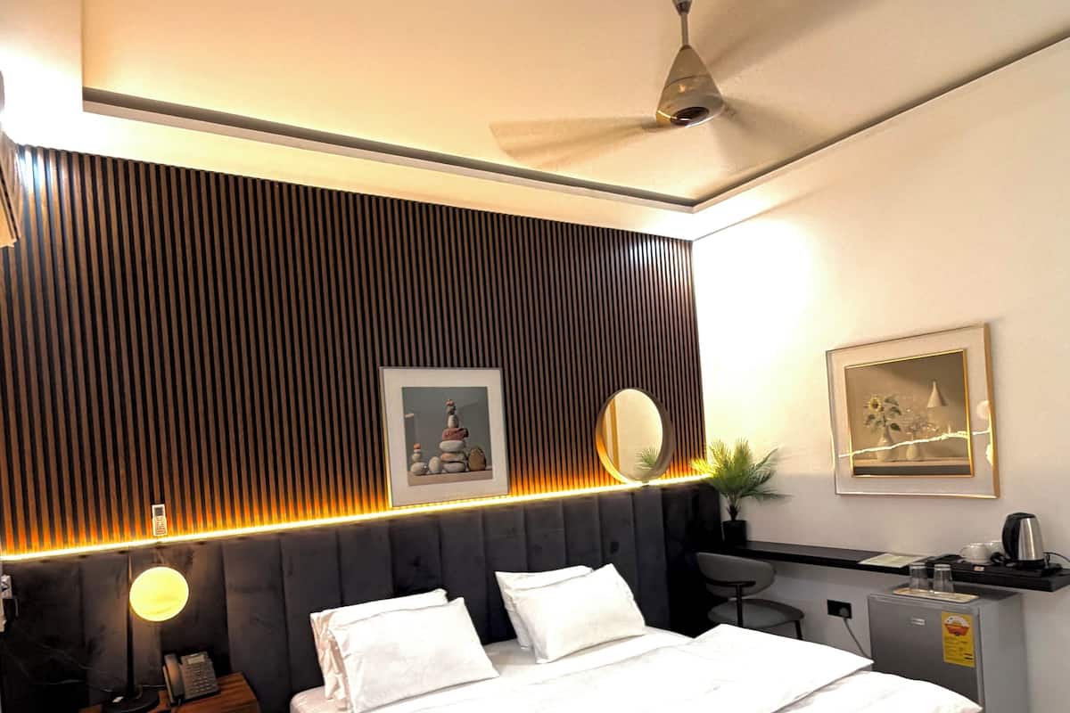 Quarto de hotel moderno com uma cama grande, uma escrivaninha, uma cadeira, uma kitchenette pequena e um ventilador de teto.