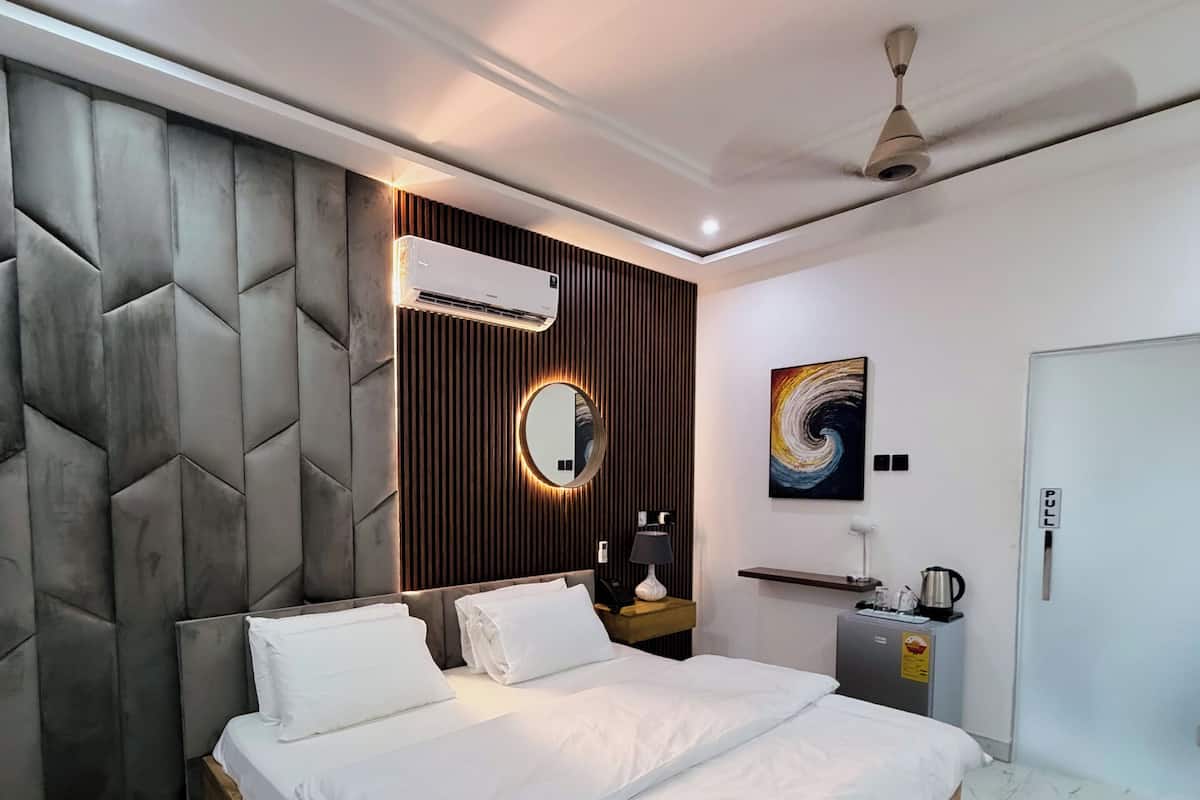 Quarto moderno com uma cama grande, ar condicionado fixado na parede, ventilador de teto, espelho redondo, um quadro e um pequeno armário.
