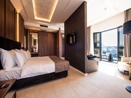 Quarto de hotel moderno com uma cama grande, televisão de tela plana, varanda com vista e uma janela ampla.