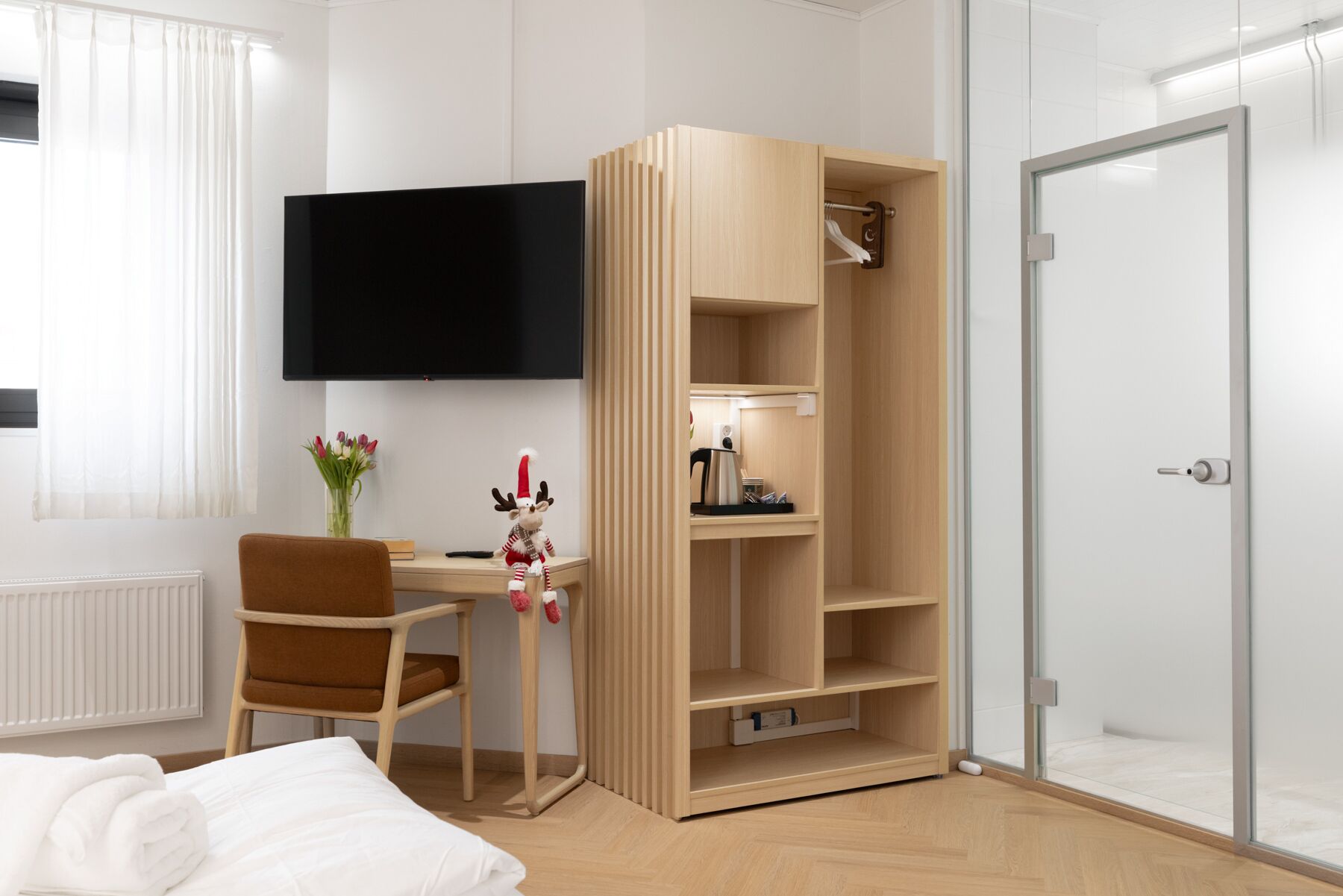 Quarto de hotel com cama, escrivaninha, guarda-roupa, televisão e zona de duche.