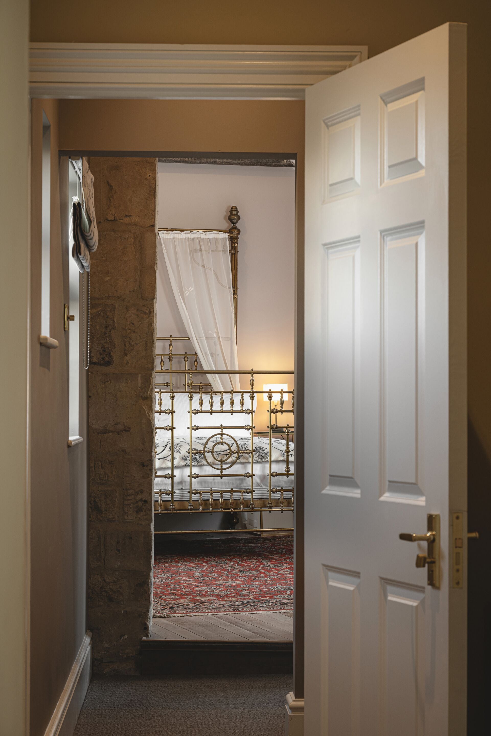 Porta de entrada para um quarto com uma cama, mesa de cabeceira e luminária.
