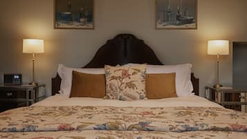 Cama bem arrumada com roupa de cama florida, duas luminárias de cabeceira e dois quadros na parede.