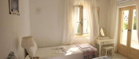 Quarto com cama, escrivaninha, cadeira, luminária e janela com cortinas.