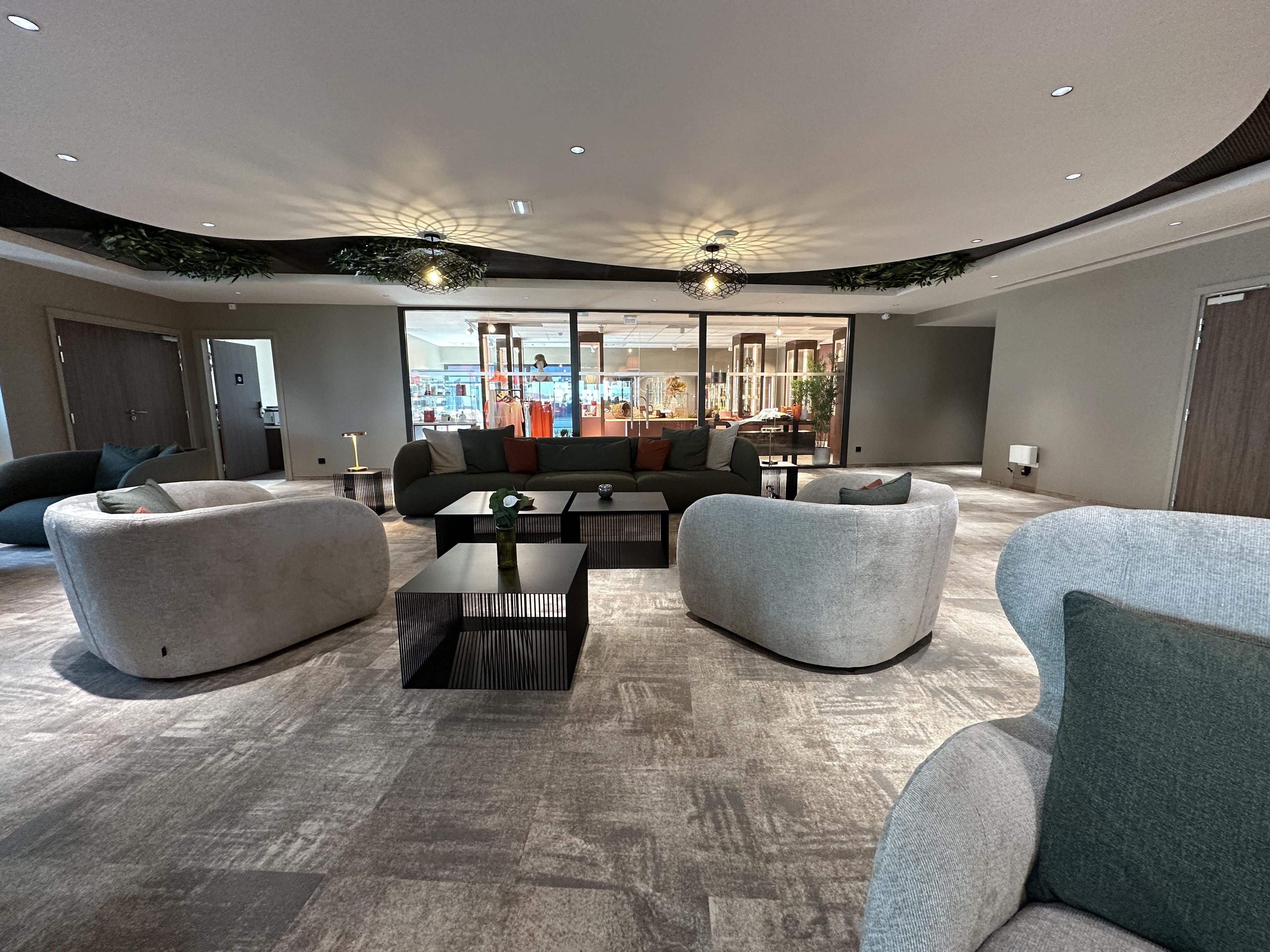 Uma sala de estar moderna com um sofá seccional, duas poltronas, uma mesa de centro e vista para uma loja através de grandes janelas.
