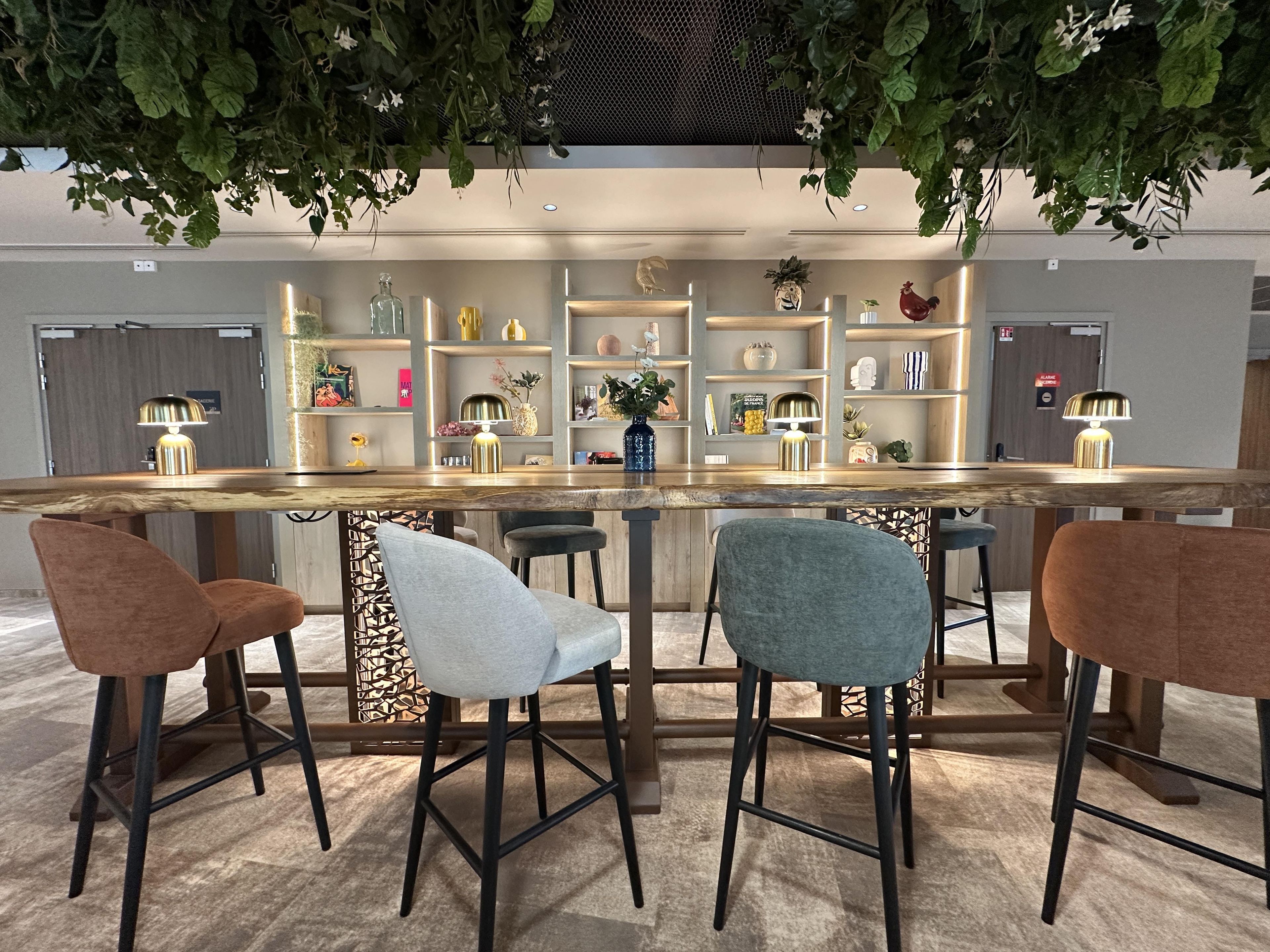 Uma área de bar moderna com balcão de madeira, banquetas e prateleiras com objetos decorativos.