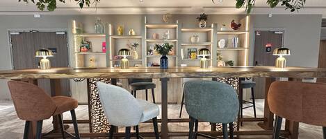 Uma área de bar moderna com balcão de madeira, banquetas e prateleiras com objetos decorativos.