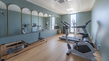 Uma academia com equipamentos de ginástica, um espelho grande e piso de madeira.