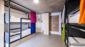 Quarto com beliche, teto de concreto, parede de tijolos e porta que dá para outro cômodo.