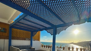 Uma área de estar coberta ao ar livre com vista para o mar ao pôr do sol.