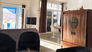 Uma sala de estar ampla com um armário de madeira grande, uma mesa de centro redonda e duas poltronas pretas.