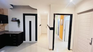 Um corredor com área de cozinha à esquerda, uma porta branca com detalhes pretos e uma porta que dá para um quarto com parede verde.