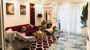 Uma sala de estar moderna com um sofá vermelho, uma poltrona cinza, um tapete estampado e um espelho grande.