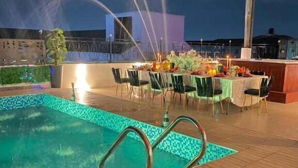 Área de piscina no terraço com mesa posta para refeições, rodeada por cadeiras, e uma piscina pequena com escada de metal.