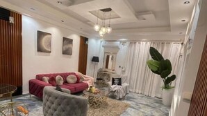 Uma sala de estar espaçosa com piso de mármore, um sofá vermelho, uma poltrona cinza e uma mesa de centro.