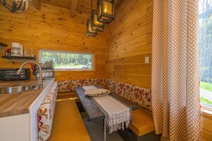 Interior de uma cabana de madeira, com cozinha, mesa de jantar e um banco.