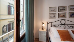 Quarto de hotel com cama, mesa de cabeceira, abajur e janela com cortinas.